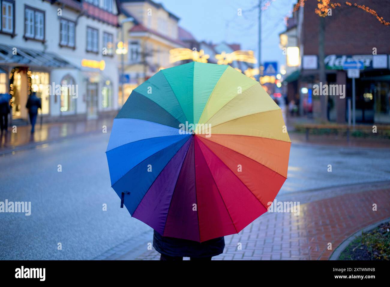 A person stands on a rainy street holding a colorful rainbow umbrella ...