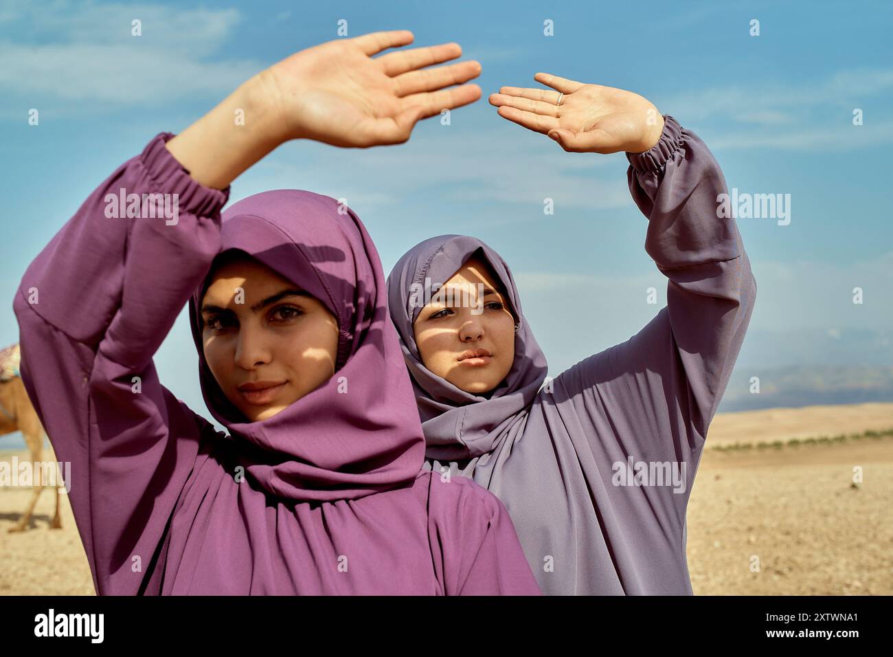 Two women in hijabs posing with their hands framing the sky in a desert ...