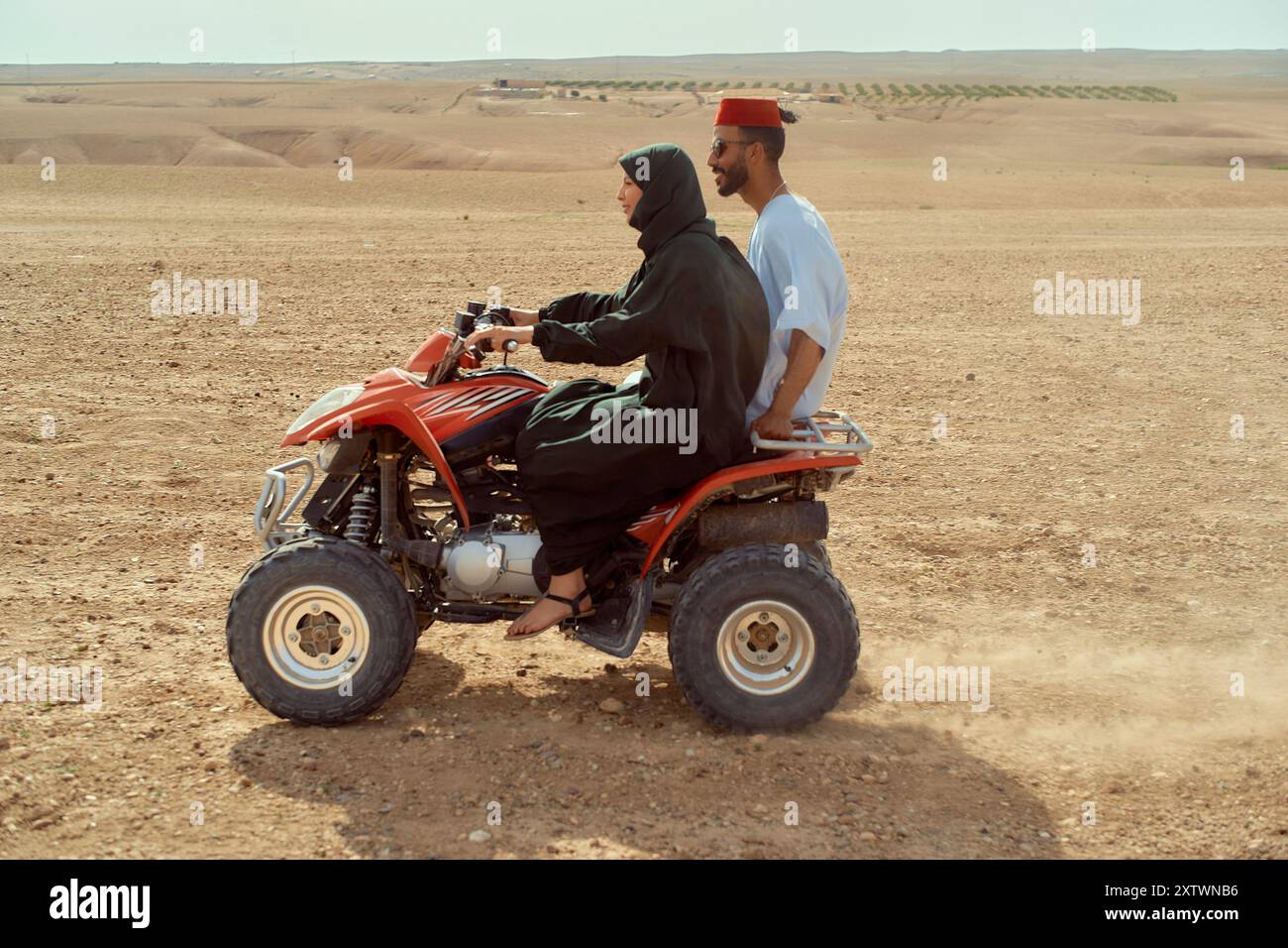 Two people riding an ATV in a desert landscape, with the driver wearing ...