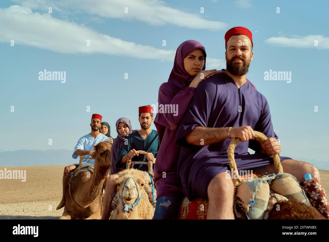 Group of people wearing traditional clothing riding camels in a desert ...