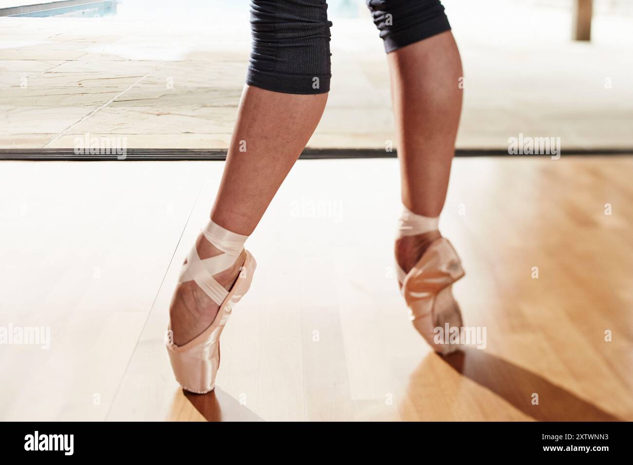 Close-up of a ballerina's feet en pointe with ballet shoes on a wooden floor, with a blurry ...