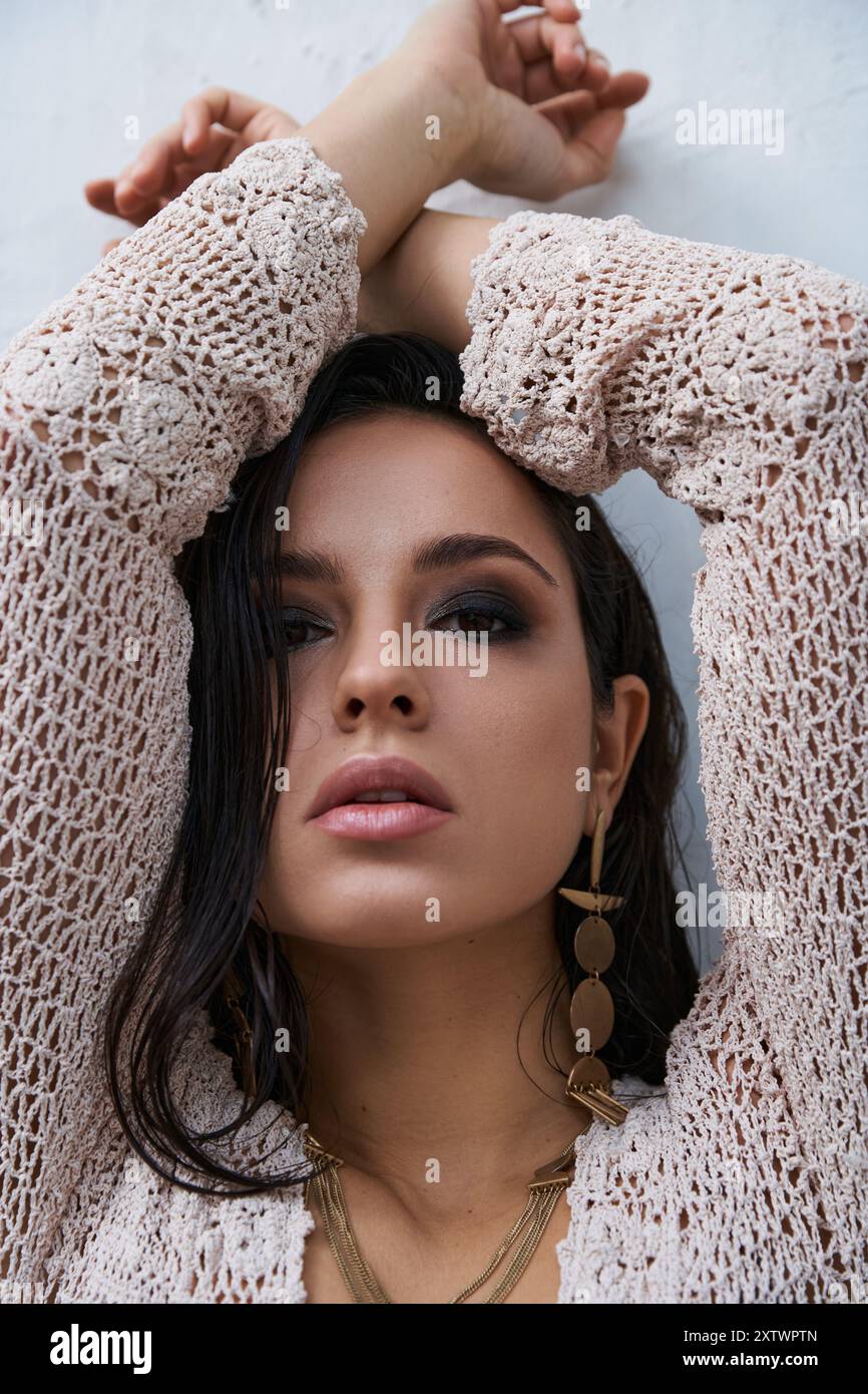 Young woman with dark hair in white knit top poses with arms crossed ...