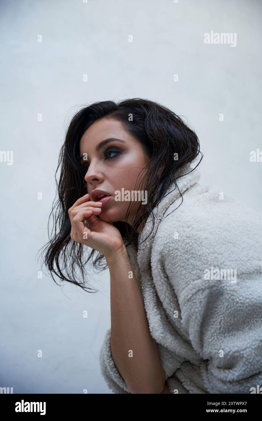 A brunette woman in a fluffy white robe, poses against a simple white ...