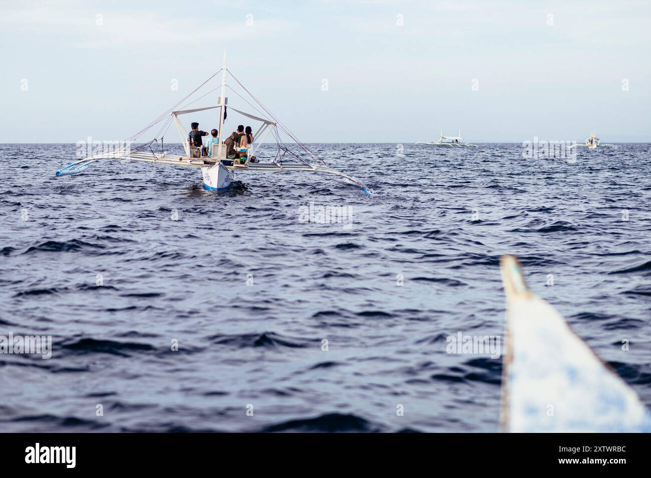 Traditional outrigger canoe sailing across the open sea with people ...