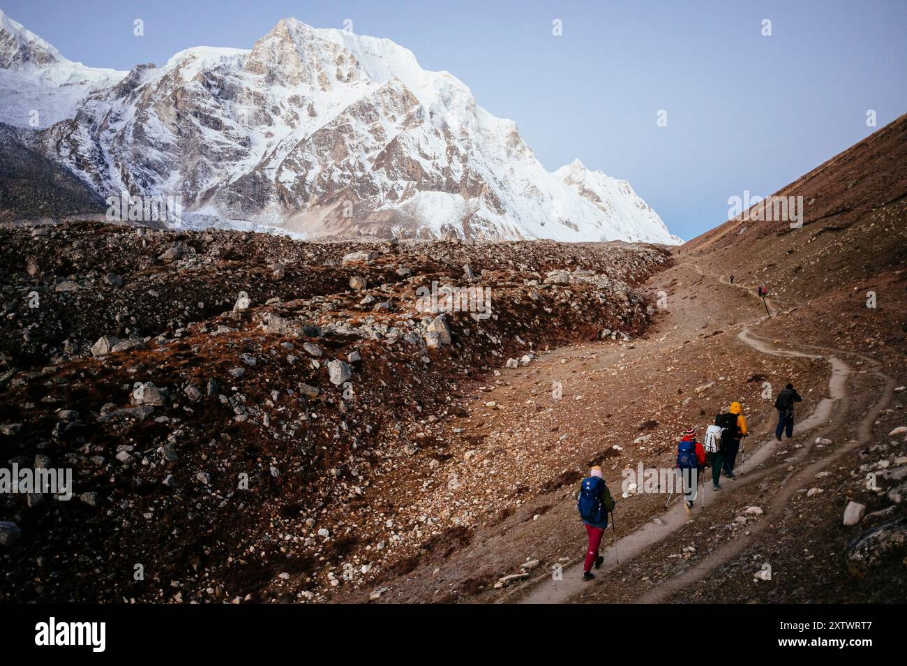 Hikers traverse a rugged mountain path with snowy peaks in the ...
