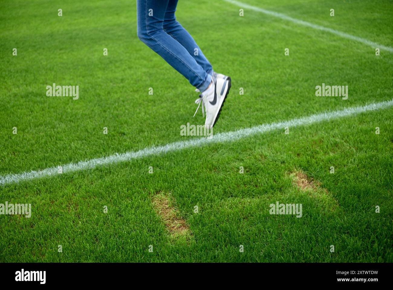 A person wearing sneakers steps onto a lush green soccer field marked ...