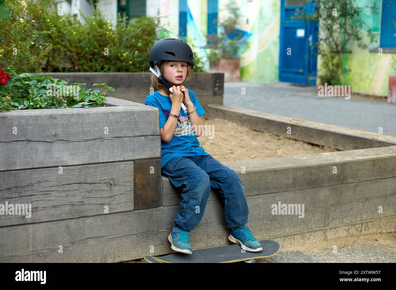 Child in a helmet sitting on a skateboard and fastening the chin strap ...