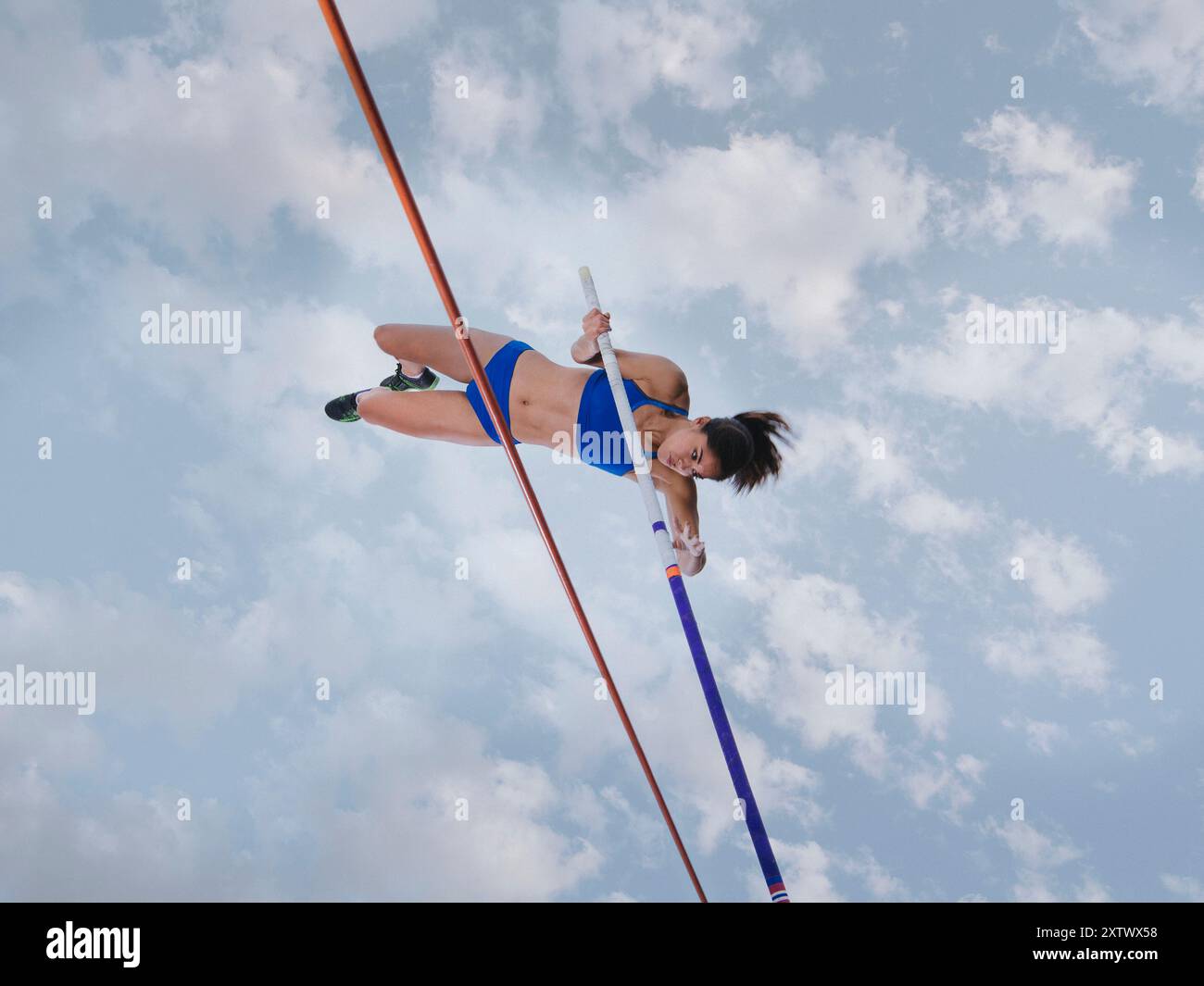 Female athlete vaulting over a high bar against a cloudy sky background ...