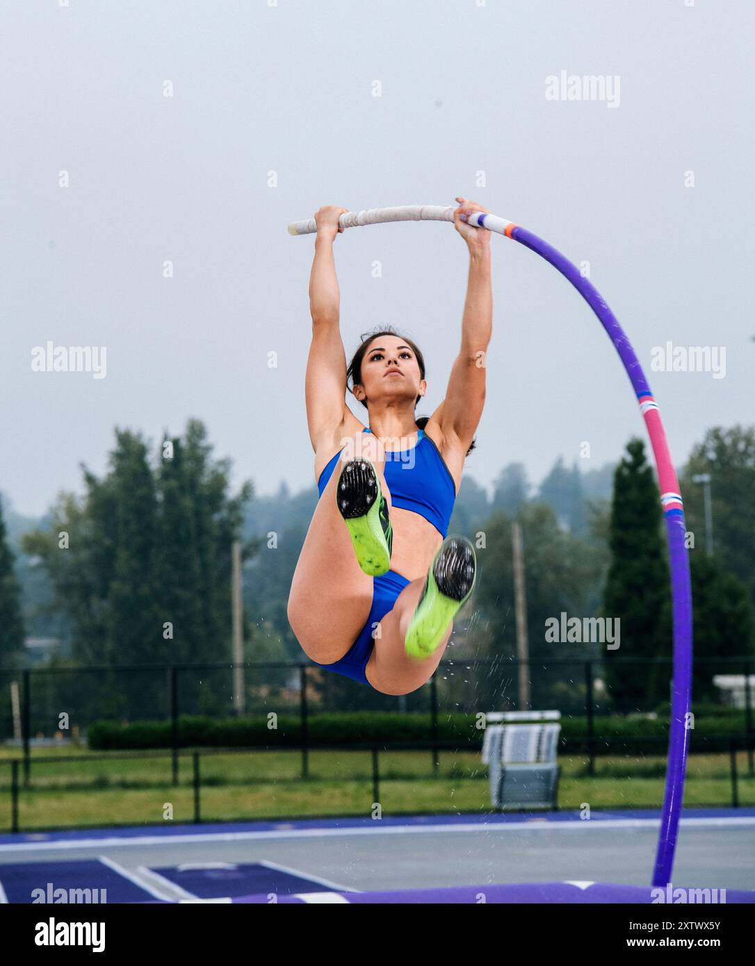Female athlete performing a high jump on an outdoor field with a cloudy sky background Stock ...