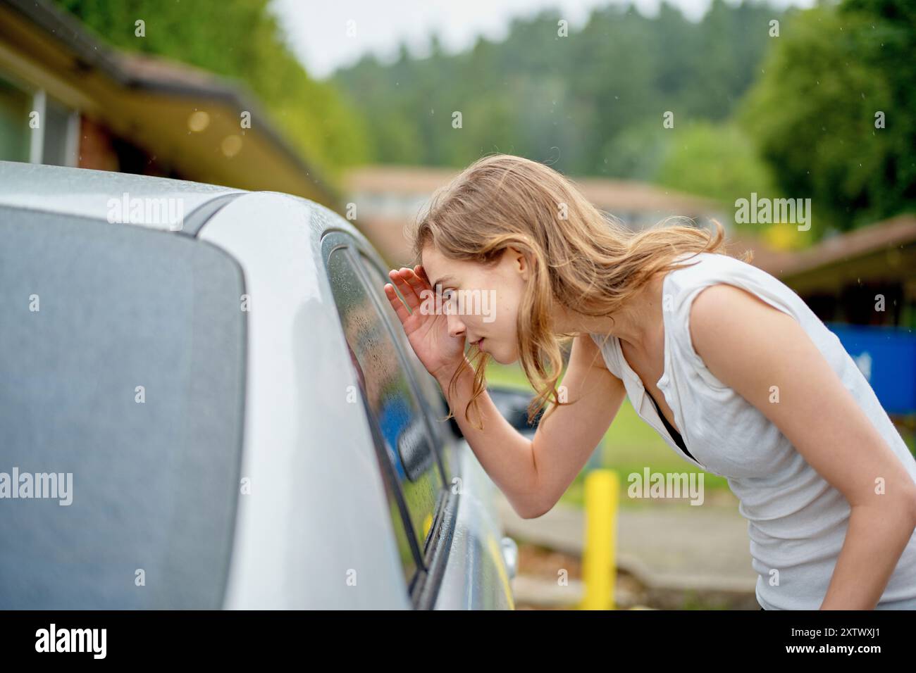 Young woman peering through a car window with a curious expression ...