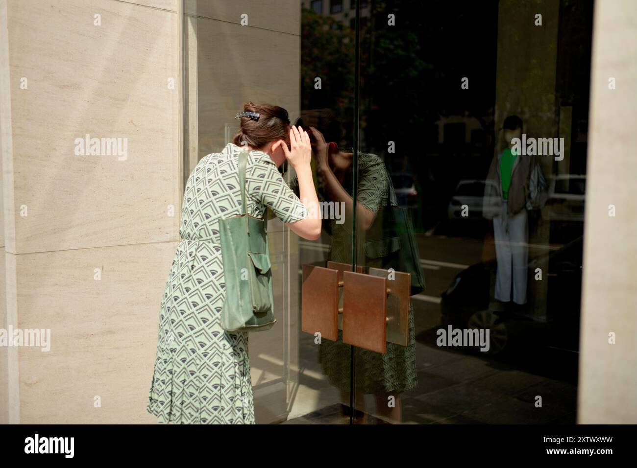 Woman in a patterned dress looking at a storefront window, her ...