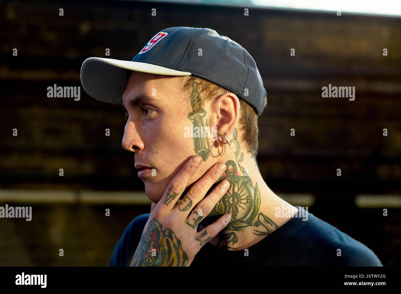 Side profile of a tattooed man in a baseball cap touching his beard ...