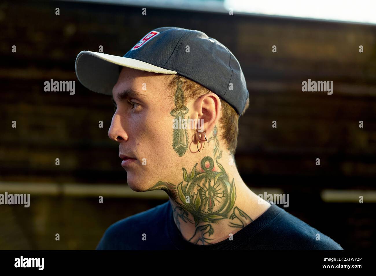 Side profile of a man with tattoos on his neck and face, wearing a baseball cap at sunset Stock ...
