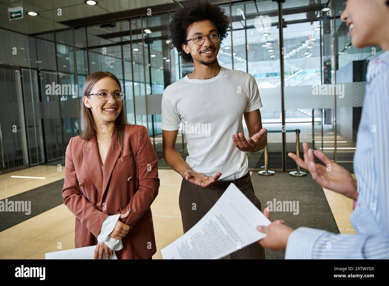 Three colleagues chat amicably in an office lobby, showcasing diversity ...