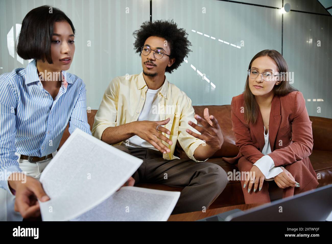 Three colleagues discuss documents while sitting on a couch in an ...