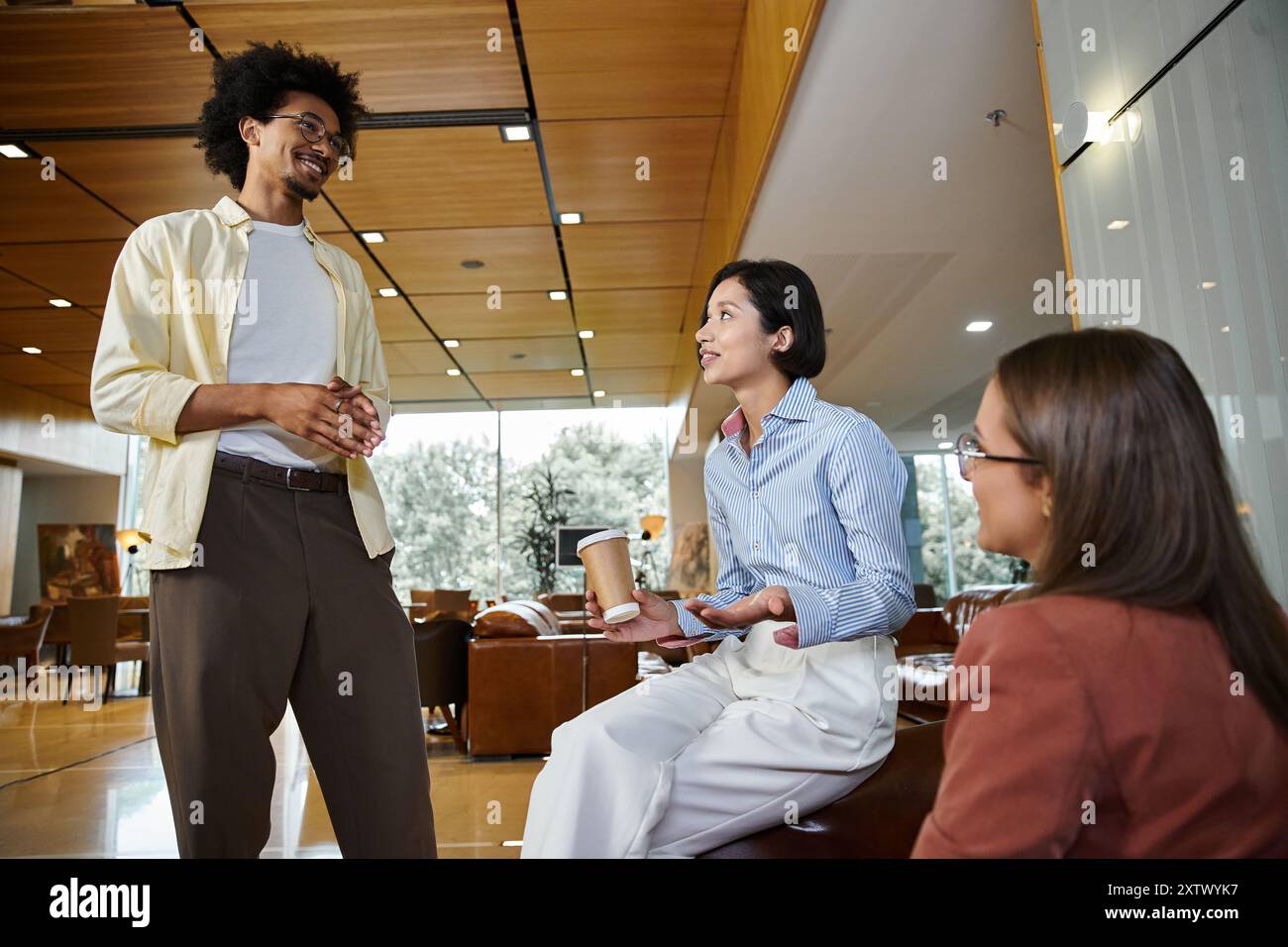 Three colleagues chat in the office lobby. One woman is holding a ...