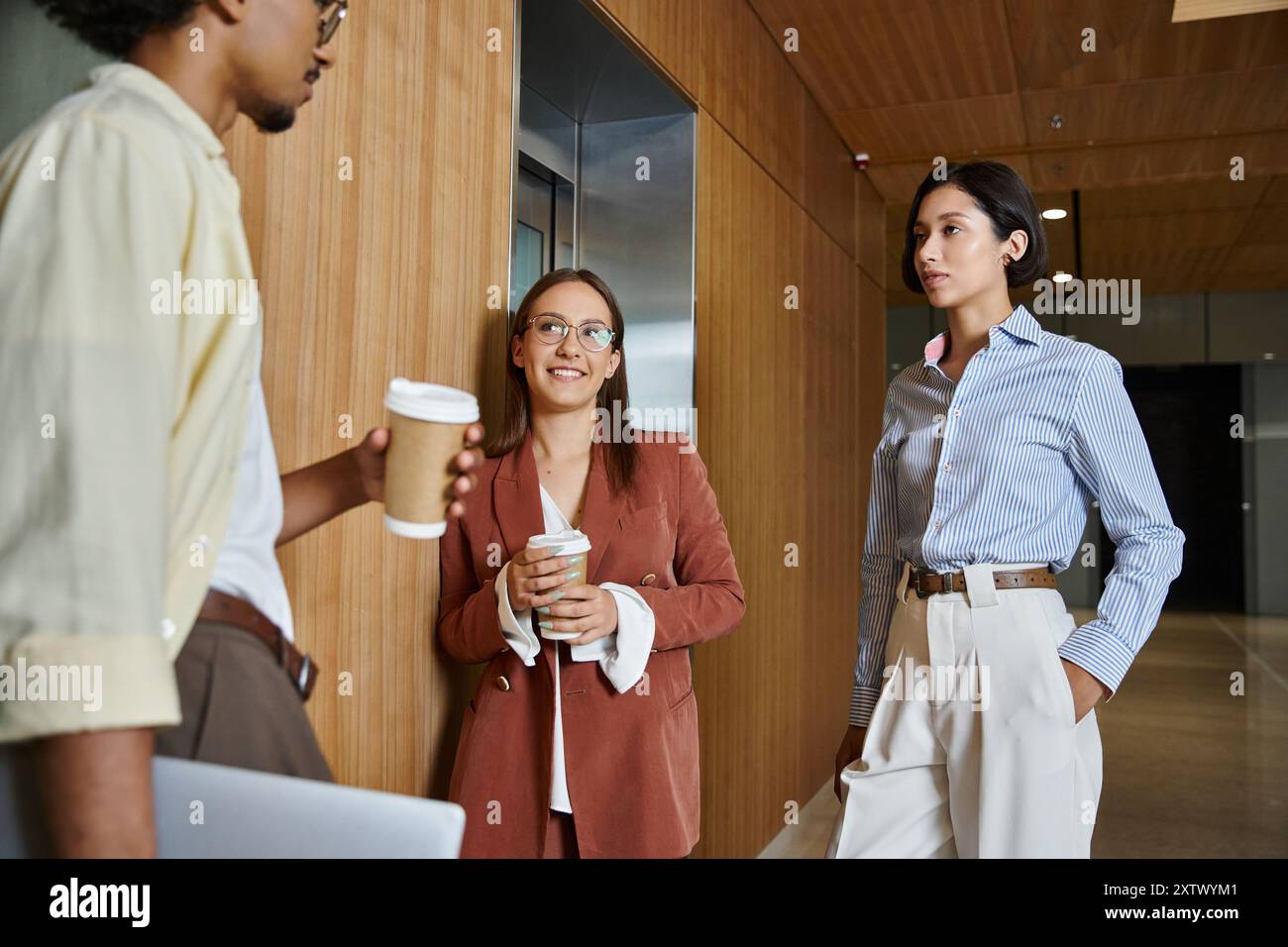 Three colleagues stand by an elevator, smiling and chatting Stock Photo ...