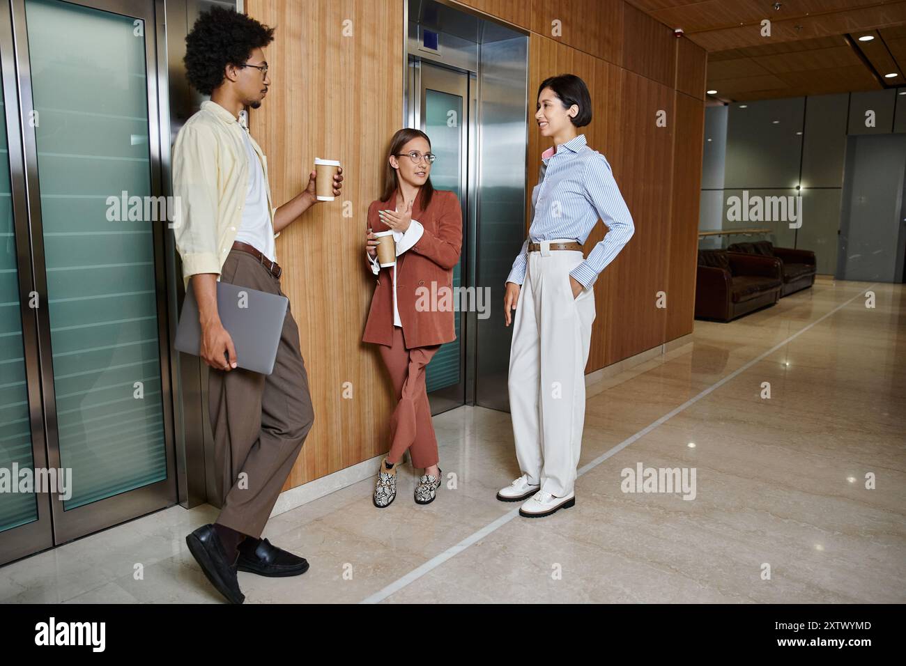 Three colleagues stand in a modern office hallway, engaging in ...