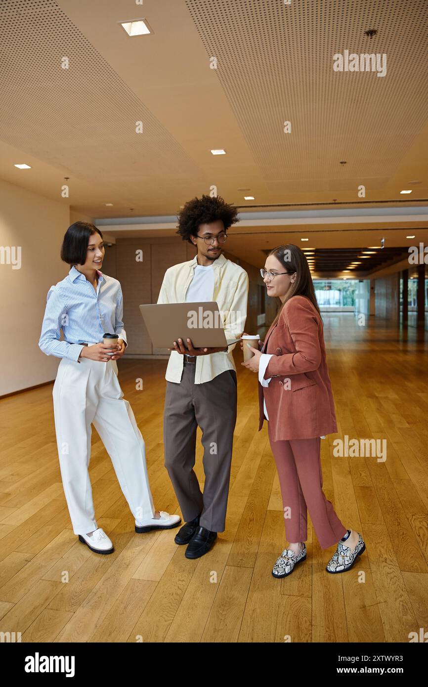 Three diverse colleagues stand in an office hallway, casually chatting ...