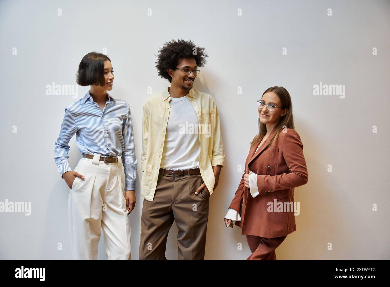 Three colleagues stand in a modern office, smiling and chatting with ...