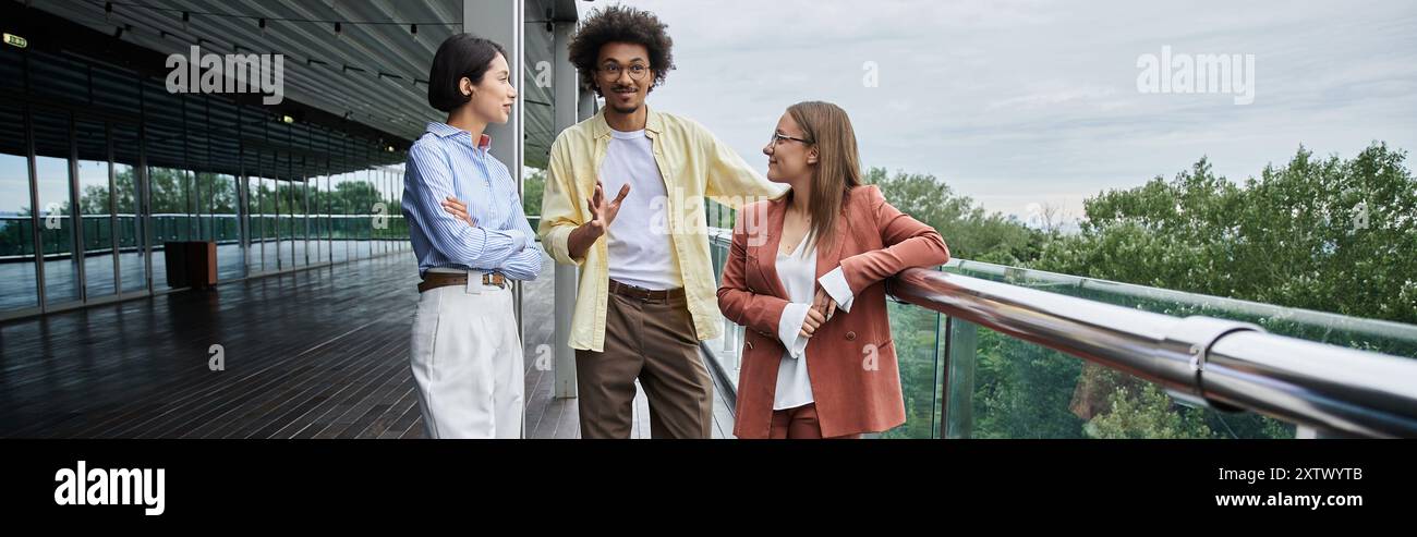 Three colleagues stand on a rooftop terrace, chatting and laughing ...
