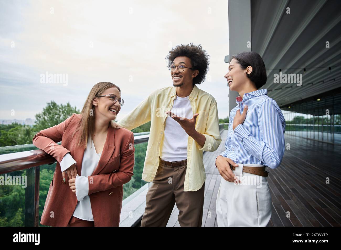 Three colleagues chat and laugh on a modern office rooftop terrace ...