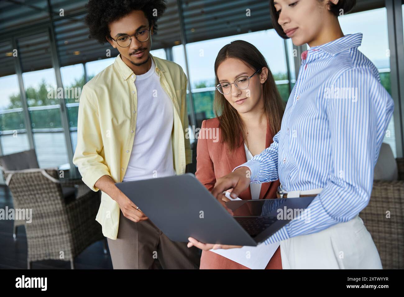 Diverse coworkers chat on a rooftop terrace, sharing a laptop and ideas ...