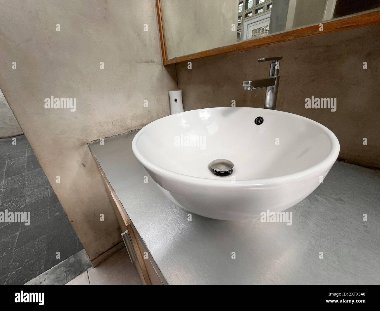 A white porcelain sink with a chrome faucet sits on a countertop. The ...