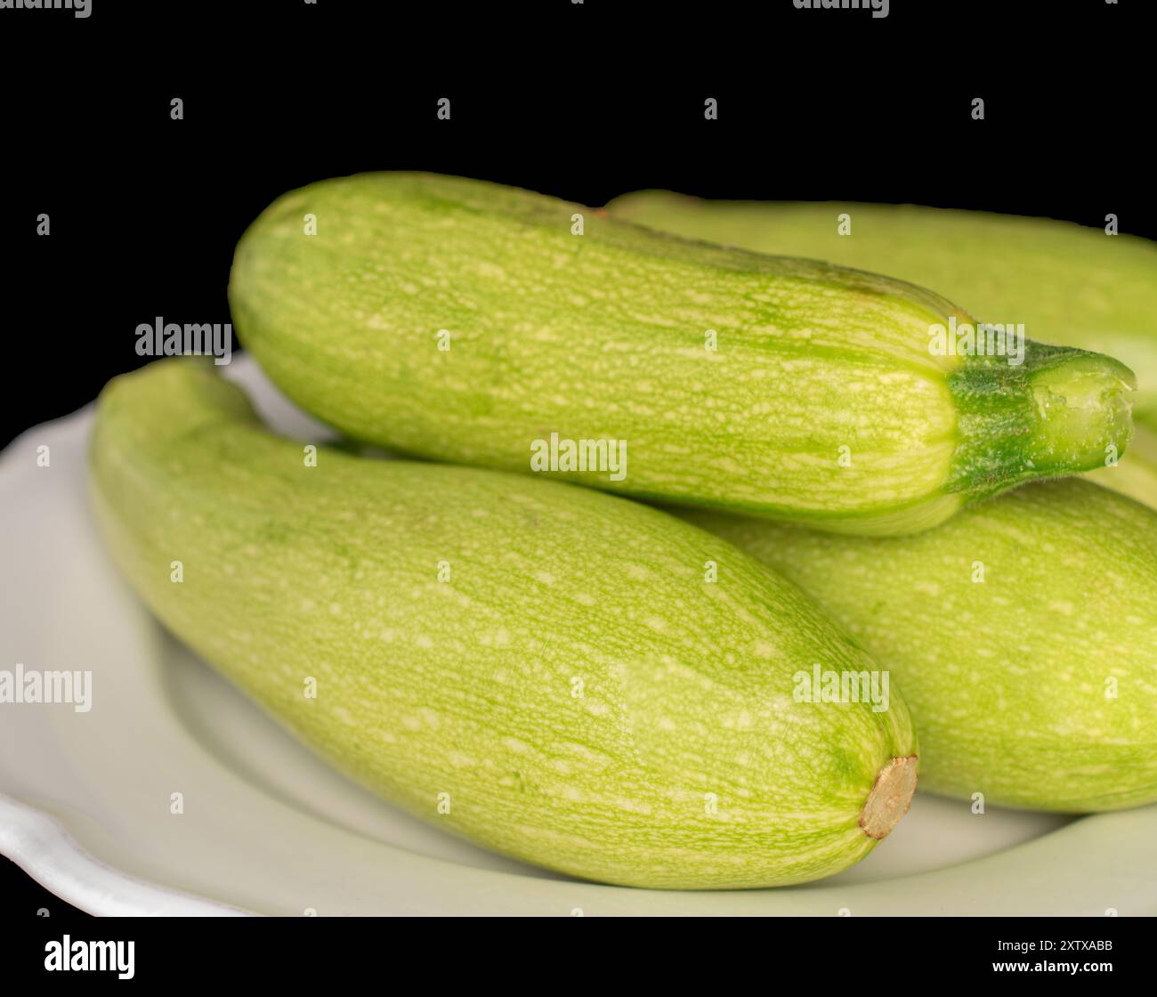 Four ripe zucchini with ceramic plate, macro, isolated on black ...