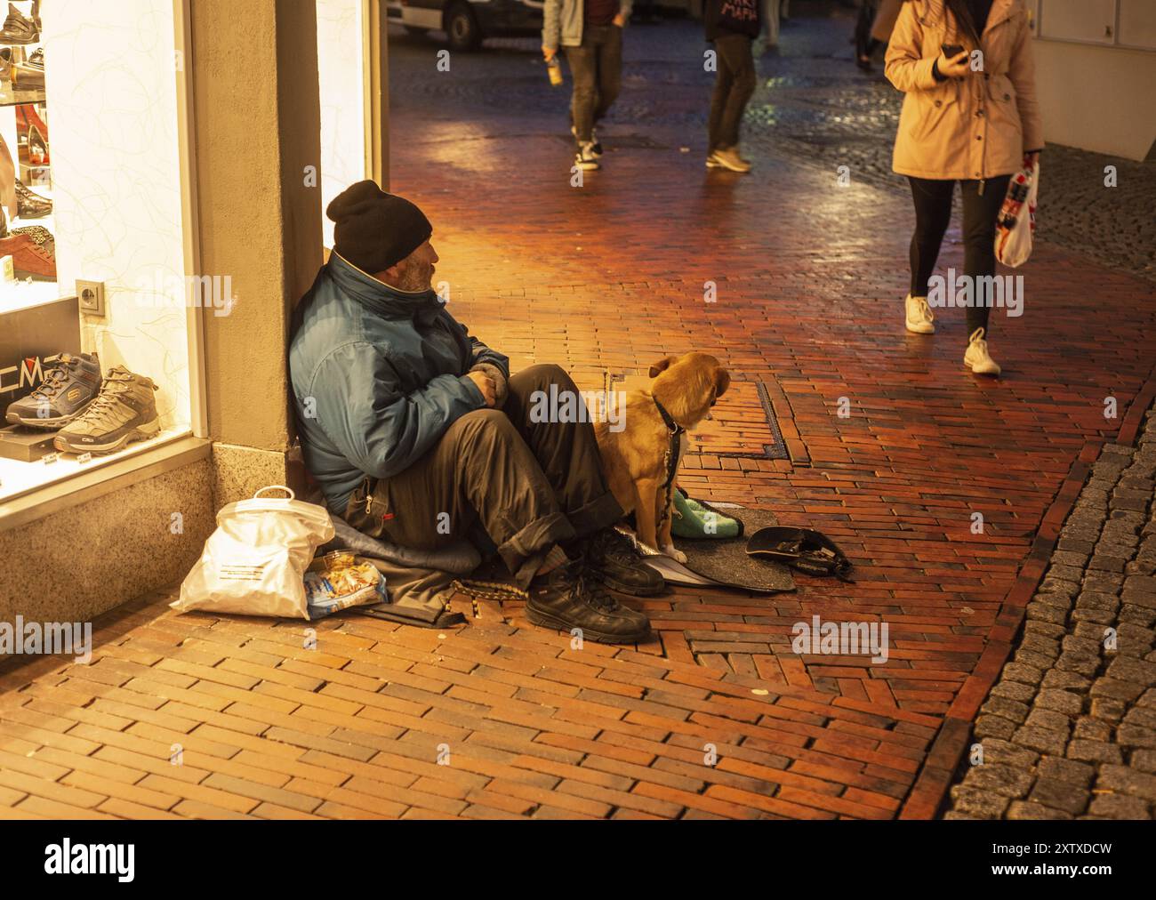 Homeless man with a dog sits in a shopping mall as people walk by in ...