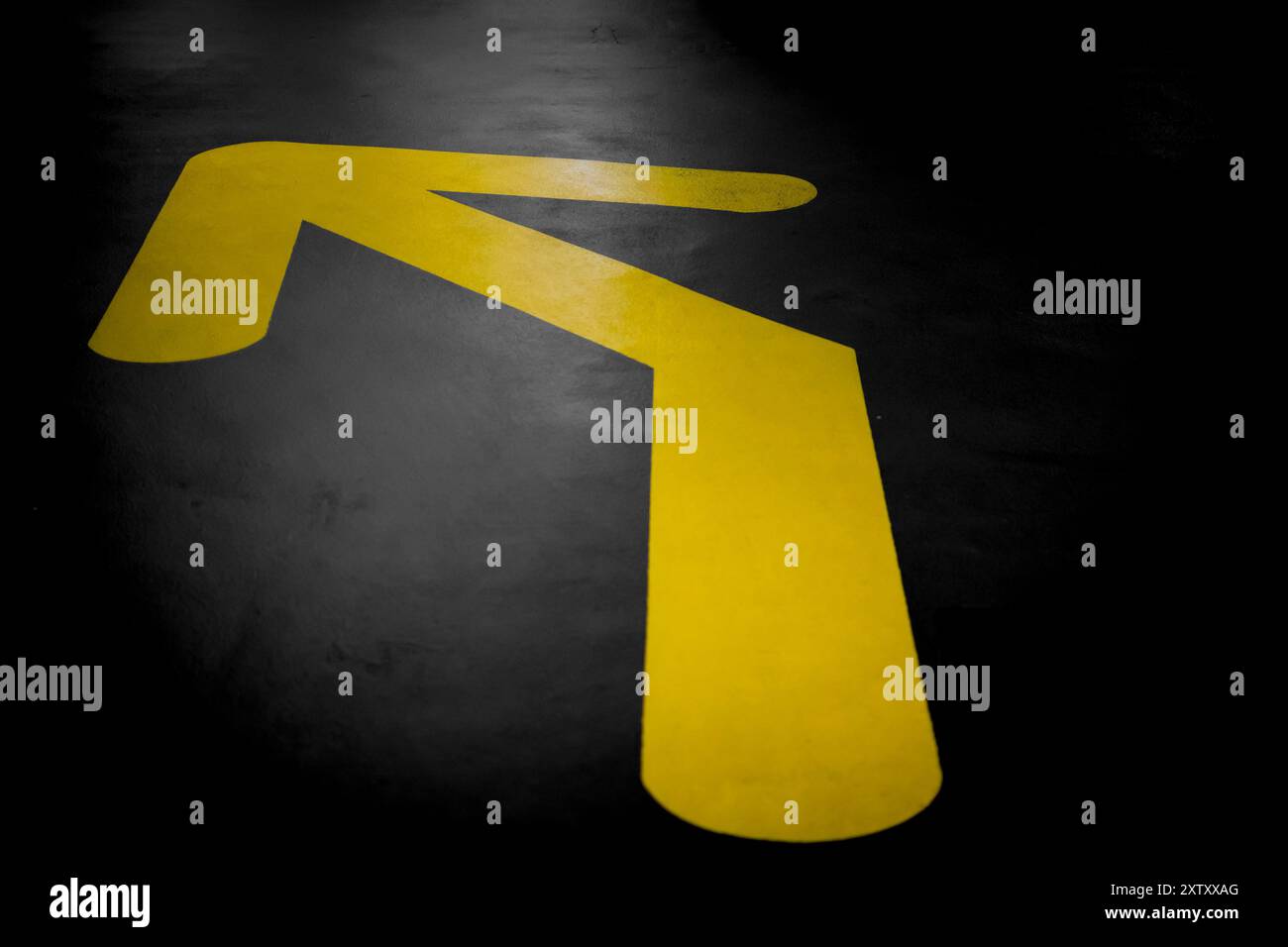 Yellow arrow on a dark asphalt surface, pointing towards the upper left ...