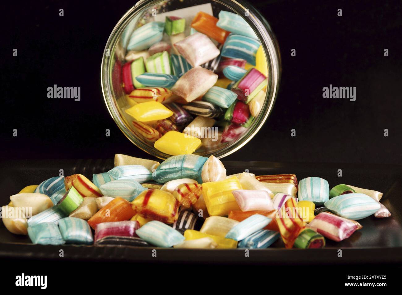 Colorful hard candies in a glass jar and on a black tray over a black ...