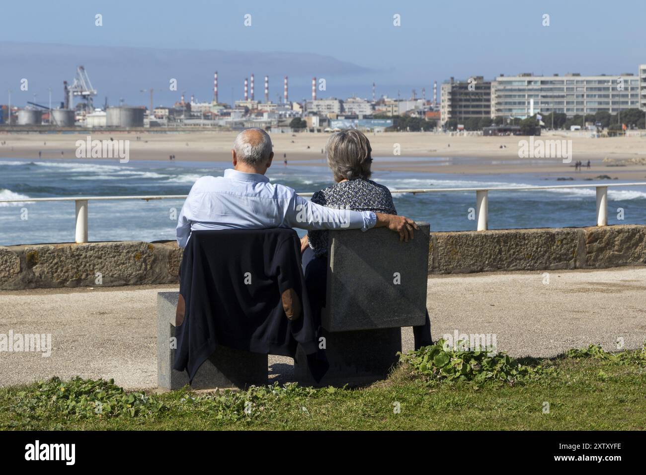 A couple of senior citizens sitting on a park bench looking at the surf ...