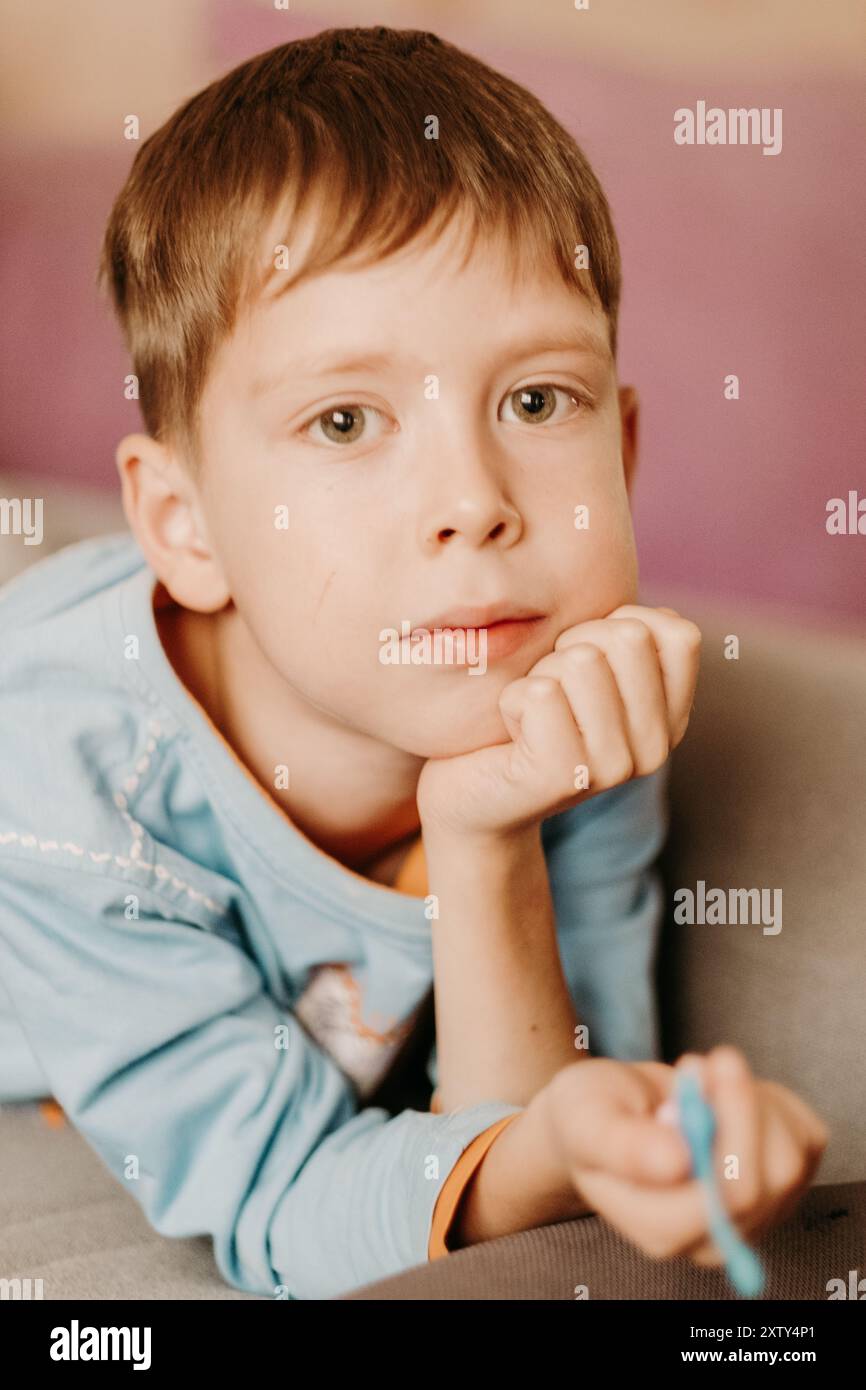 Cute 10 year old boy lies on his stomach on the sofa and looks at the ...