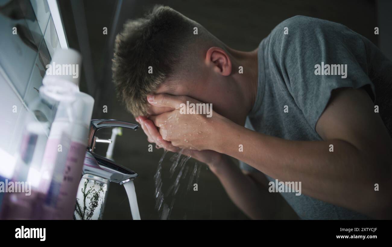 Caucasian boy comes to sink in bathroom, washes face with cold water ...