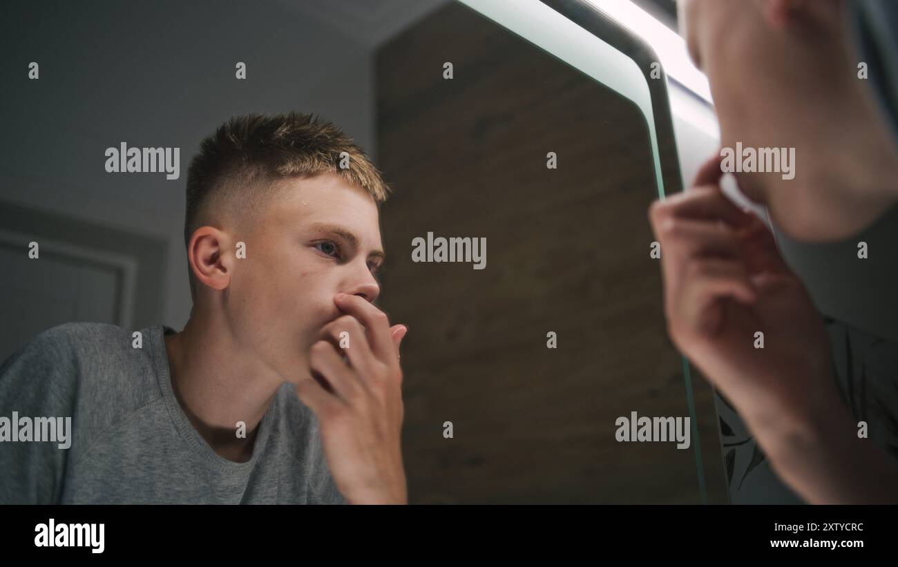 Caucasian boy stands in bathroom and looks at his reflection in the ...