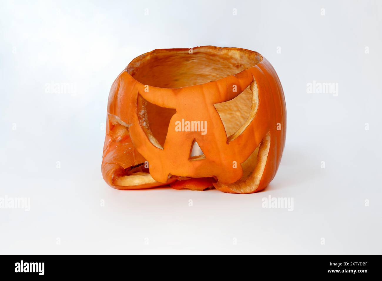A collapsed Jack-o'-lantern with a deteriorating face on a white ...