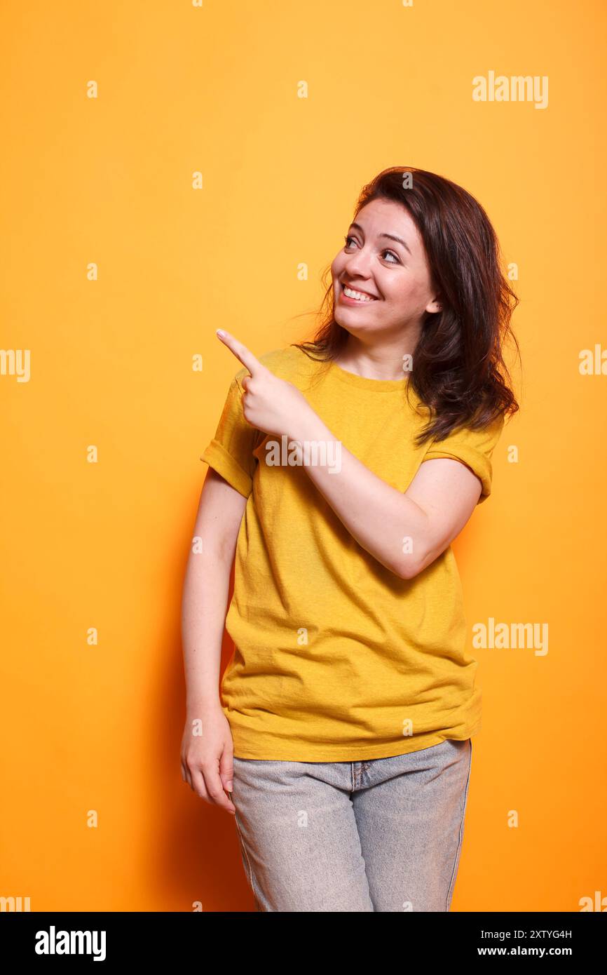 Beautiful lady standing in front of isolated orange background pointing ...