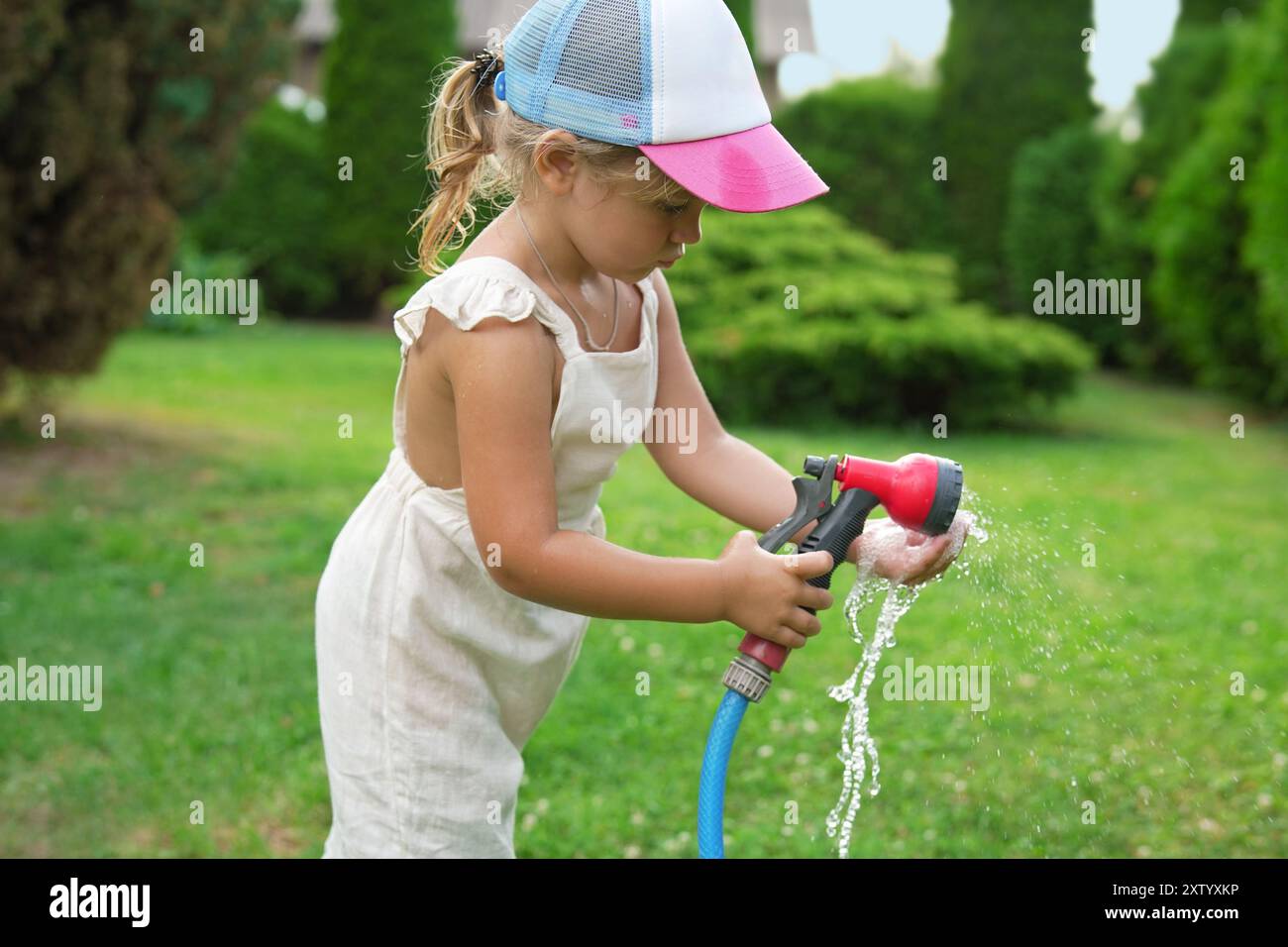 Little girl watering lawn with hose in backyard Stock Photo - Alamy