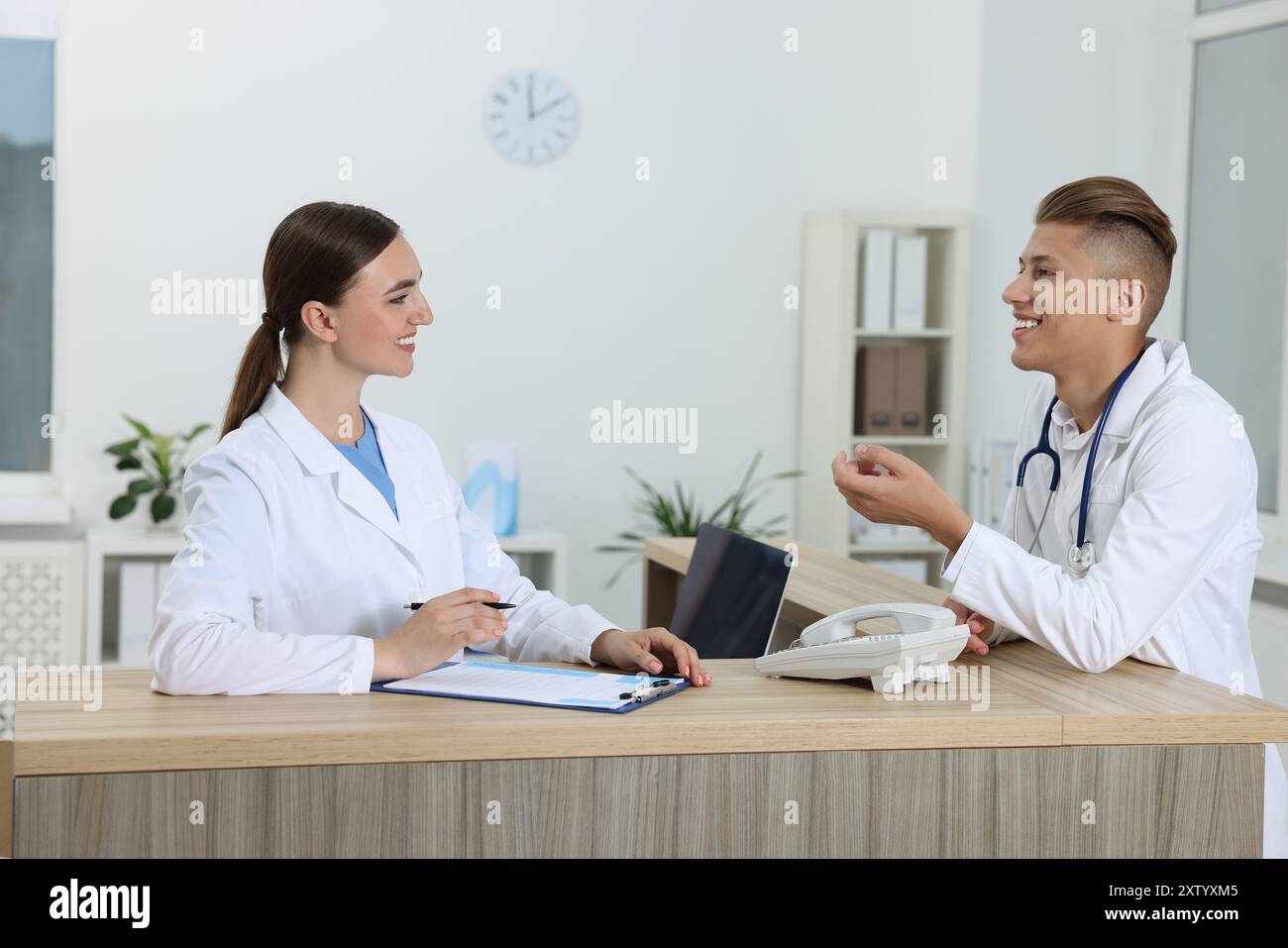 Professional receptionist and doctor at wooden desk in hospital Stock ...
