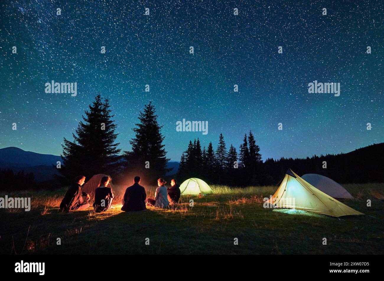 Group of friends hikers resting around campfire, surrounded by ...