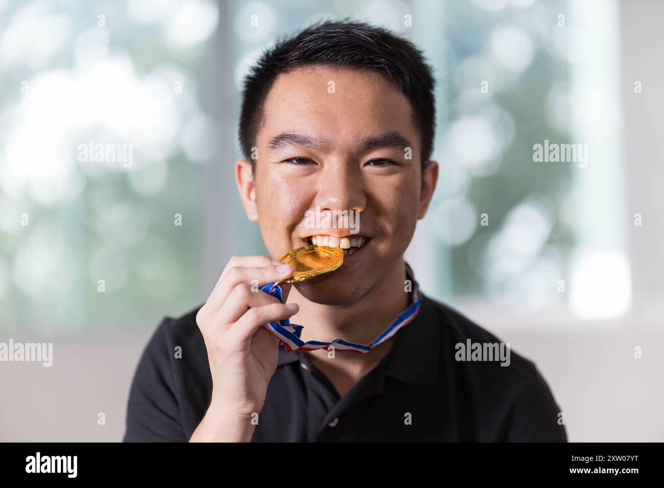 A young teenage boy is biting his gold medal as a pose after his ...