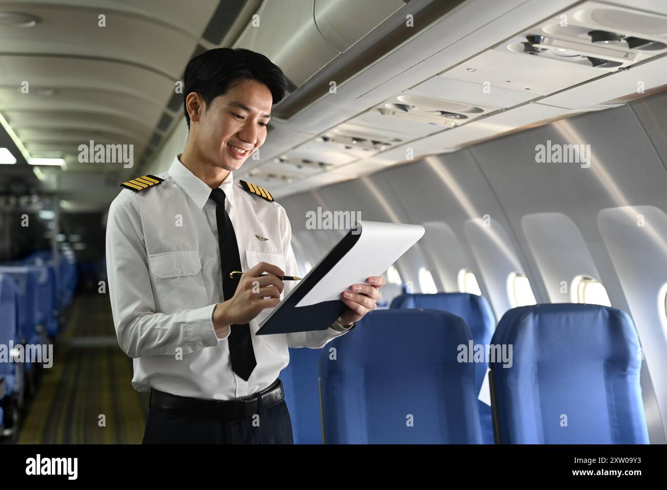 Portrait of smiling pilot with clipboard standing in the aisle of an ...