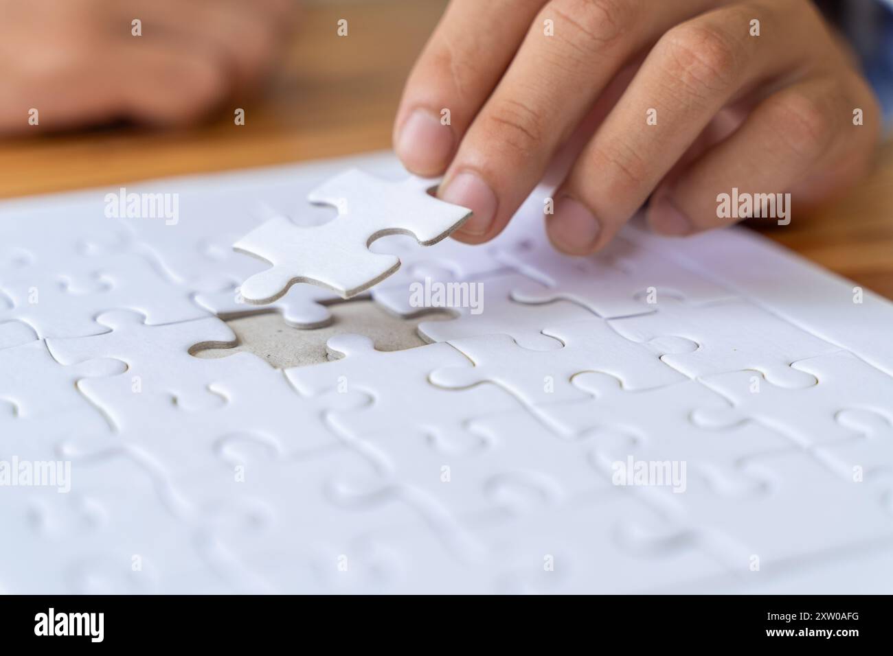 Close up hand of a man holding a white jigsaw puzzle piece trying to ...