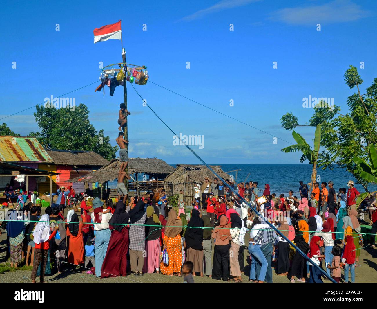 A panjat pinang competition by the sea, with a blue sky and ocean as ...
