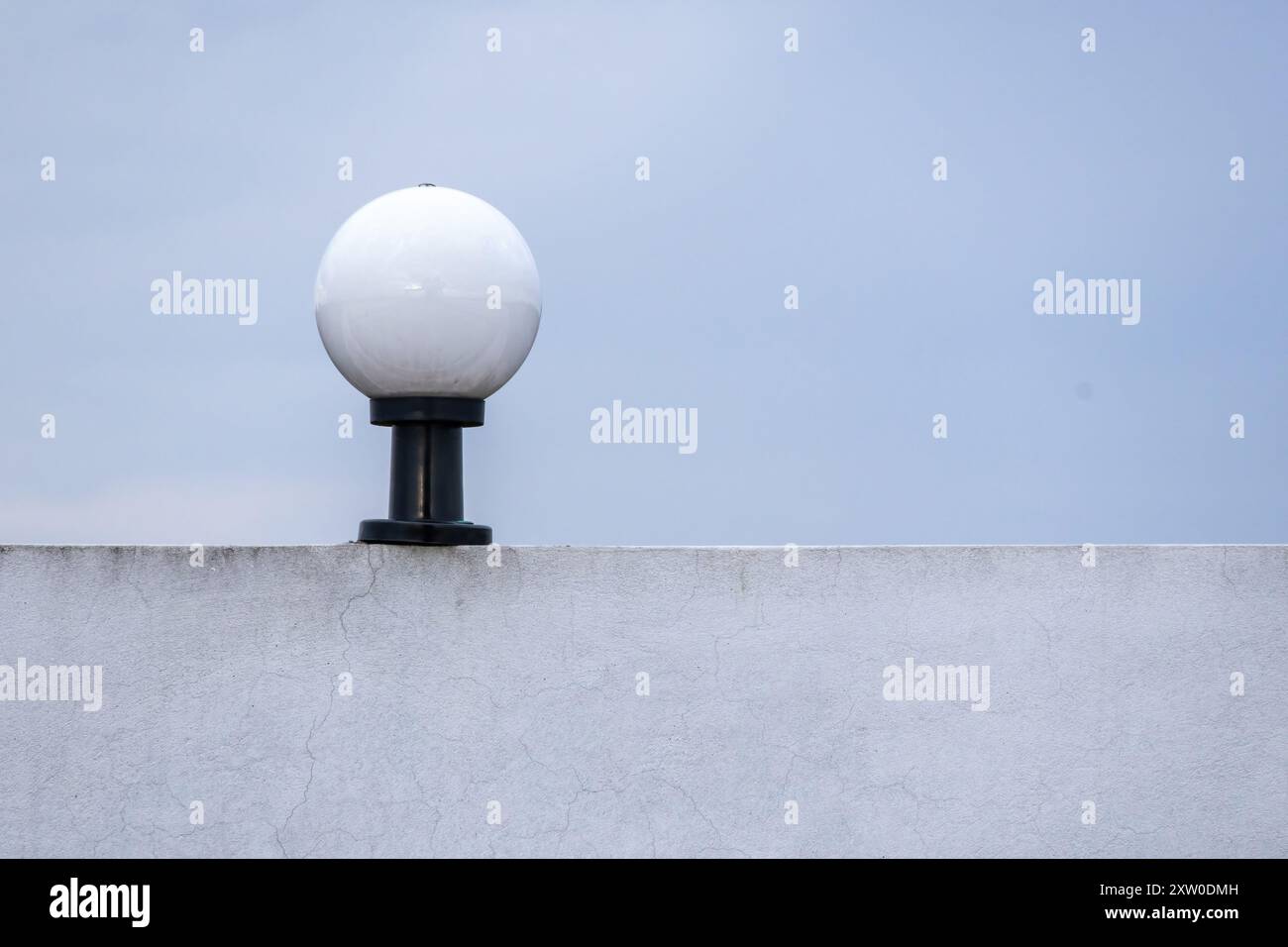 White round glass lamp on a black steel pole on the house wall, light ...