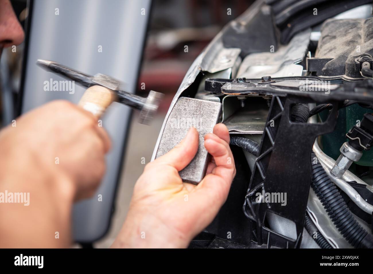 A skilled mechanic focuses intently while using a hammer to shape a ...