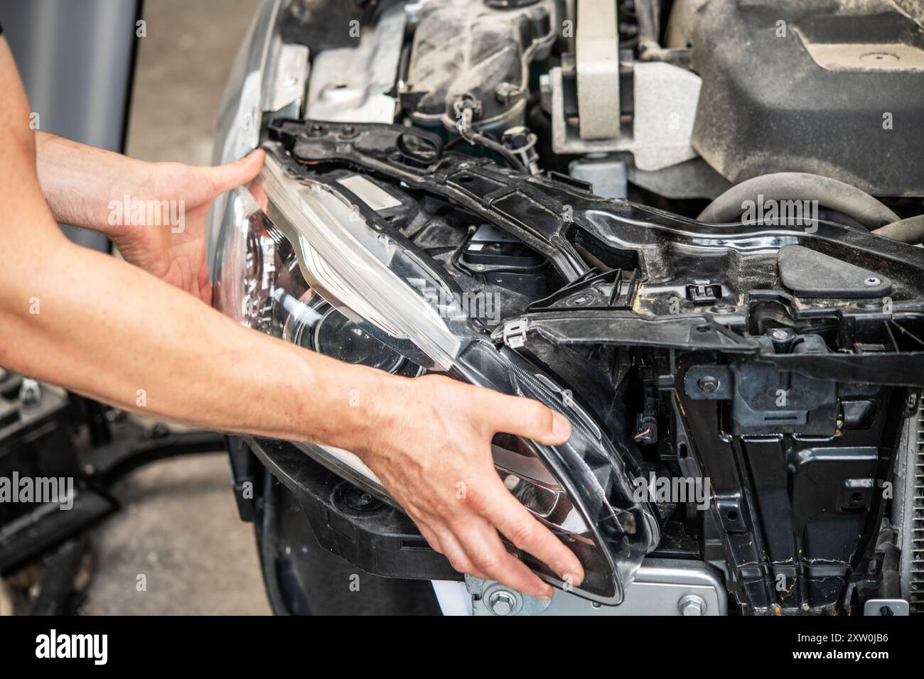 An experienced mechanic carefully installs a new headlight in a car's ...