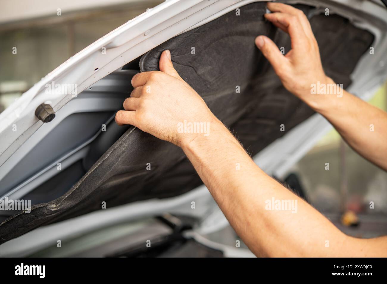 A mechanic's hands carefully remove and replace underhood insulation in ...