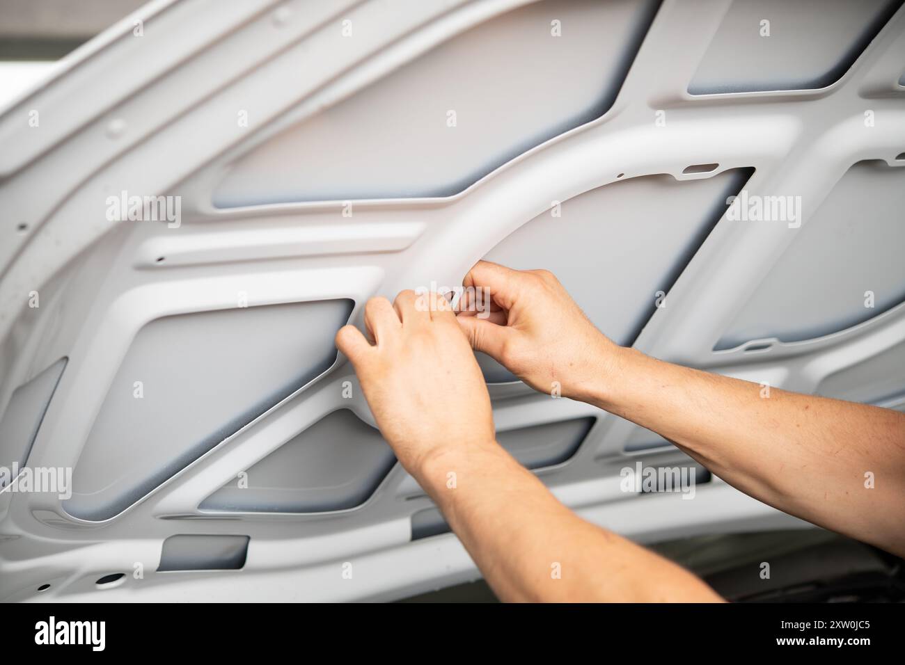 A focused individual is performing maintenance inside a car hood ...